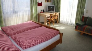 Um quarto com uma cama, uma escrivaninha com televisão, uma cadeira e um sofá.