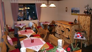 Uma área de jantar acolhedora com mesas e bancos de madeira, um armário de madeira com acabamento rústico e uma janela com cortinas.