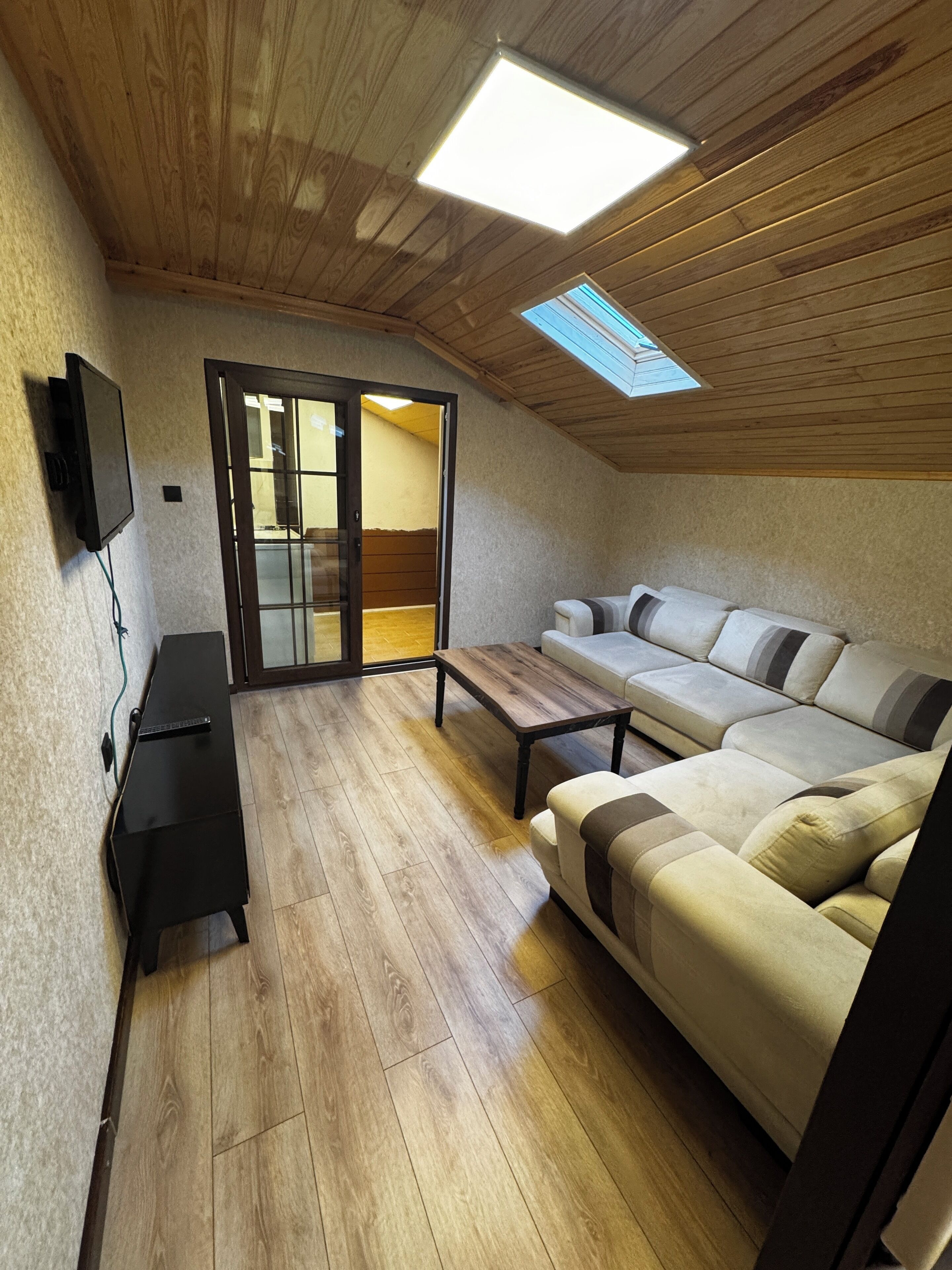 Um quarto de sótão acolhedor com teto de madeira, um sofá, uma mesa de centro e uma televisão.