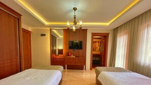 Quarto de hotel com duas camas, televisão, cómoda de madeira e um candelabro.