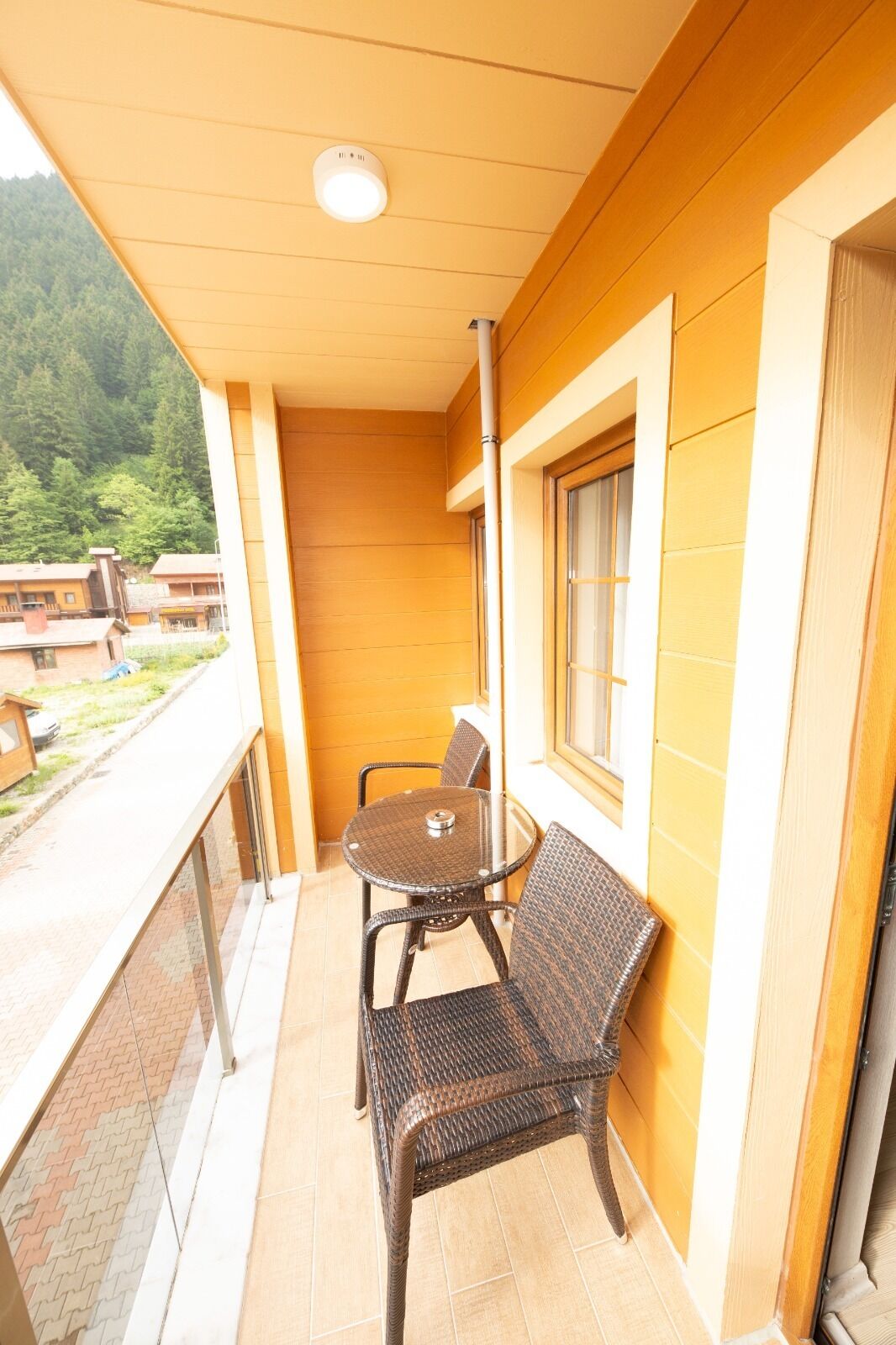 Varanda com mesa, cadeiras, uma janela e vista para uma área arborizada.