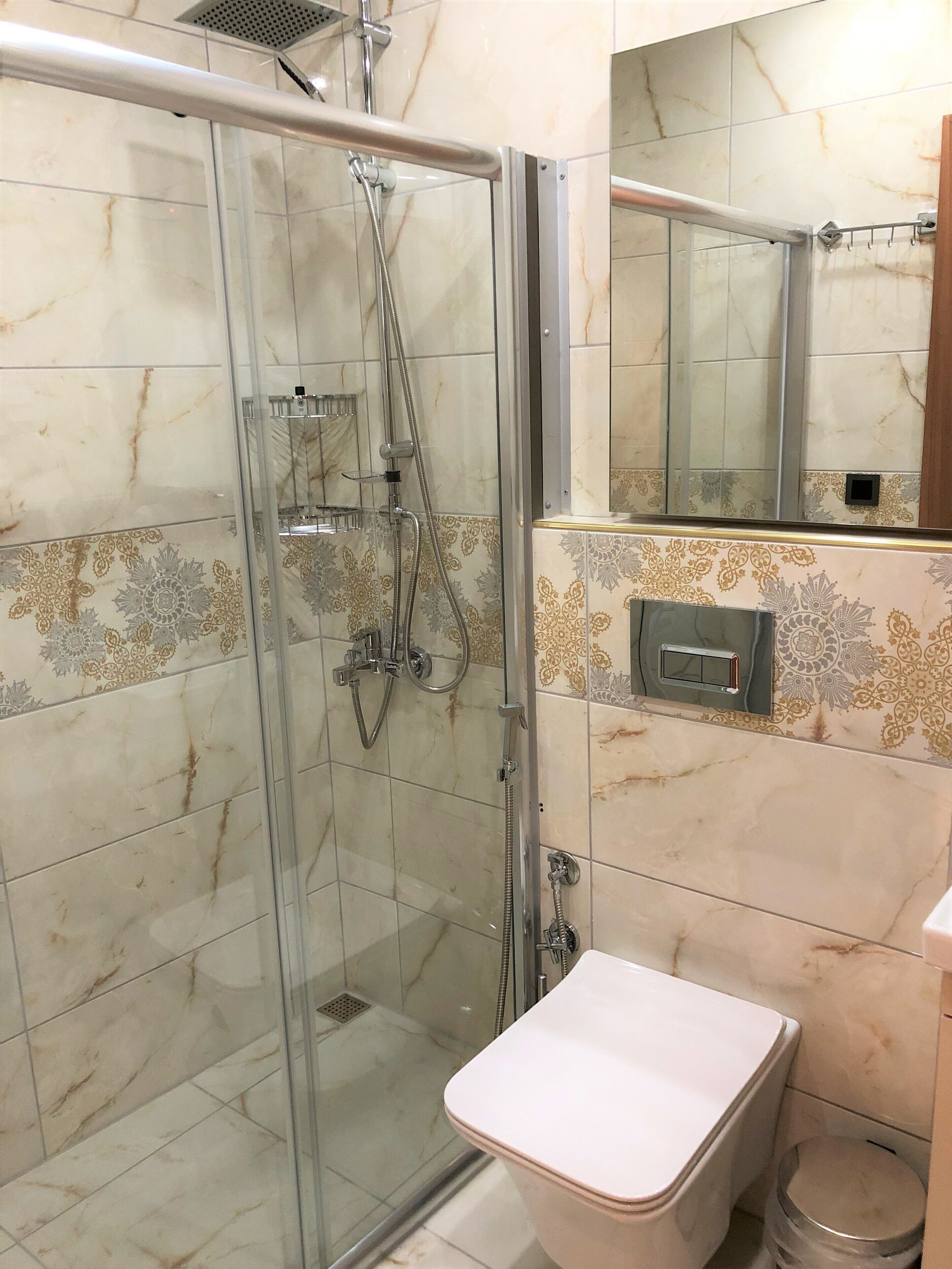 Um banheiro com chuveiro em box de vidro, vaso sanitário e pia.