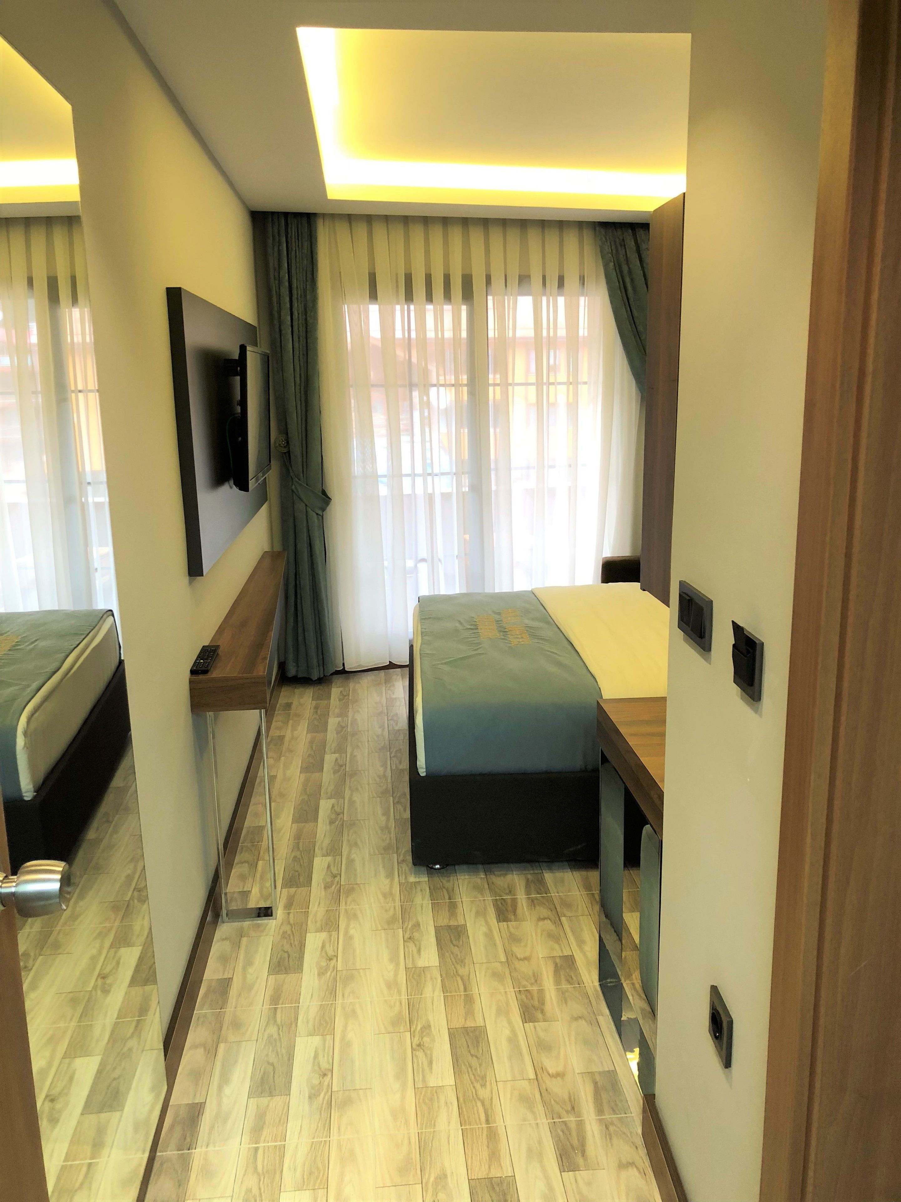 Quarto de hotel com duas camas, uma televisão de tela plana na parede, uma escrivaninha com cadeira e uma janela com cortinas.