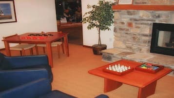 Uma sala de estar acolhedora com lareira, uma mesa de jantar com cadeiras e uma mesa de centro com peças de xadrez.