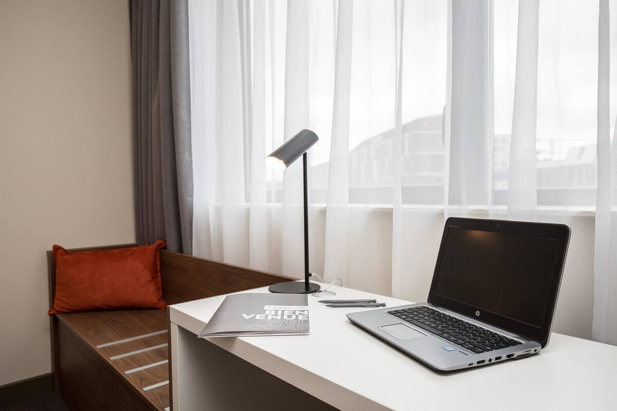 Um laptop numa secretária com um livro intitulado 'VENICE COME' e uma lâmpada.