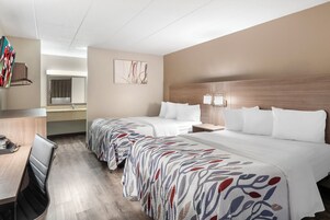 Quarto de hotel com duas camas, uma escrivaninha, uma cadeira, um espelho e uma obra de arte na parede.