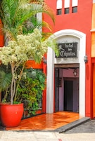 Entrada de um hotel com fachada vermelha, uma grande planta em vaso e uma placa com a inscrição 'hotel las Cúpulas'.
