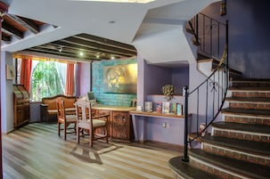 Uma área de refeições com uma mesa e cadeiras de madeira, uma parede de tijolos com um mural e uma escada com grades decorativas.