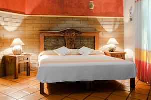 Uma cama bem arrumada com colcha e travesseiros brancos, cabeceira de madeira e duas mesas de cabeceira com abajures.