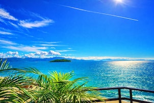 Uma praia tropical com águas azul-claras, uma ilha ao longe e um sol brilhante.