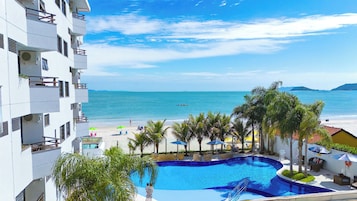 Um hotel com piscina, vista para a praia e palmeiras.