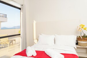 Quarto de hotel com uma cama grande, varanda com uma cadeira e vista para o mar.