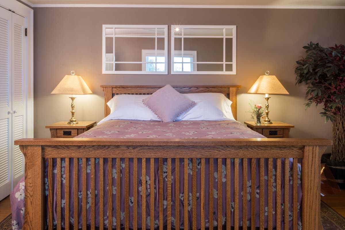Uma cama de madeira com colcha florida, duas luminárias de cabeceira e um espelho sobre a cama.