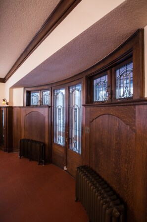 Um corredor com portas e janelas de madeira, um radiador e piso revestido de azulejos.