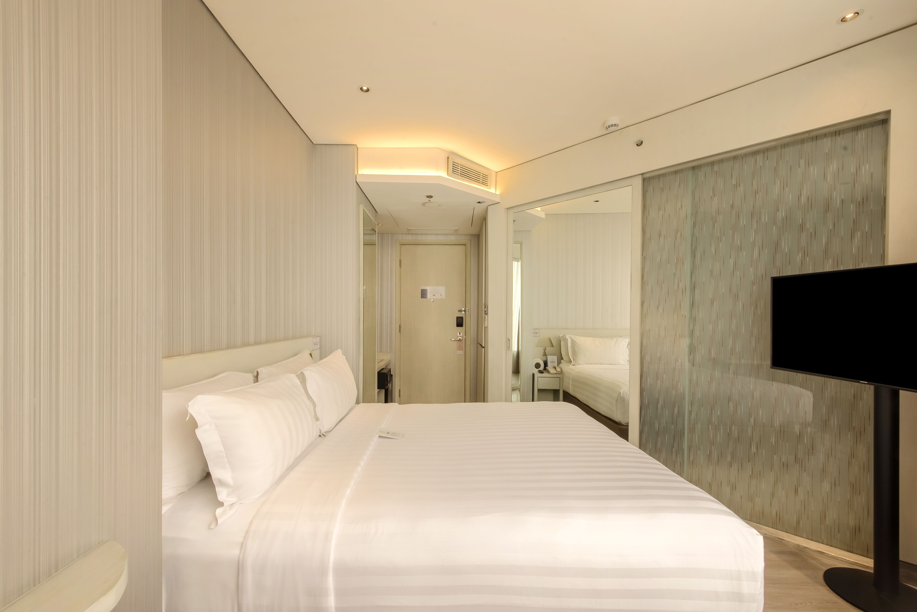 Quarto de hotel moderno com uma cama grande, televisão de tela plana, mesa de cabeceira e closet espaçoso.
