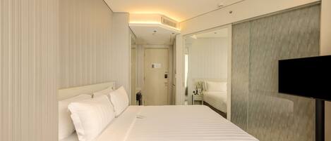 Quarto de hotel moderno com uma cama grande, televisão de tela plana, mesa de cabeceira e closet espaçoso.