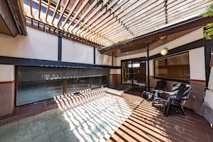 Área externa iluminada pelo sol, com uma pérgola de madeira, uma estrutura de vidro e duas cadeiras Adirondack.
