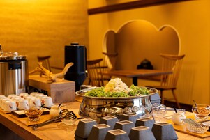 Disposição de buffet com um grande prato de prata, várias tigelas e utensílios sobre uma mesa de madeira.