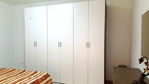 Quarto com guarda-roupa espaçoso, cama com colcha listrada e mesa de cabeceira pequena com objeto decorativo.