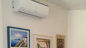 Uma sala de estar com sofá bege, um aparelho de ar condicionado e três quadros na parede.
