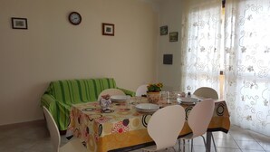 Uma área de refeições com uma mesa posta para quatro pessoas, um sofá verde e uma toalha de mesa florida.