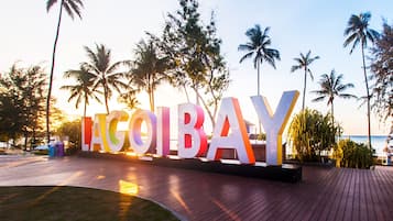 Um grande e colorido letreiro com a inscrição "LAGOBAY" em primeiro plano, com palmeiras e um deck de madeira ao fundo.