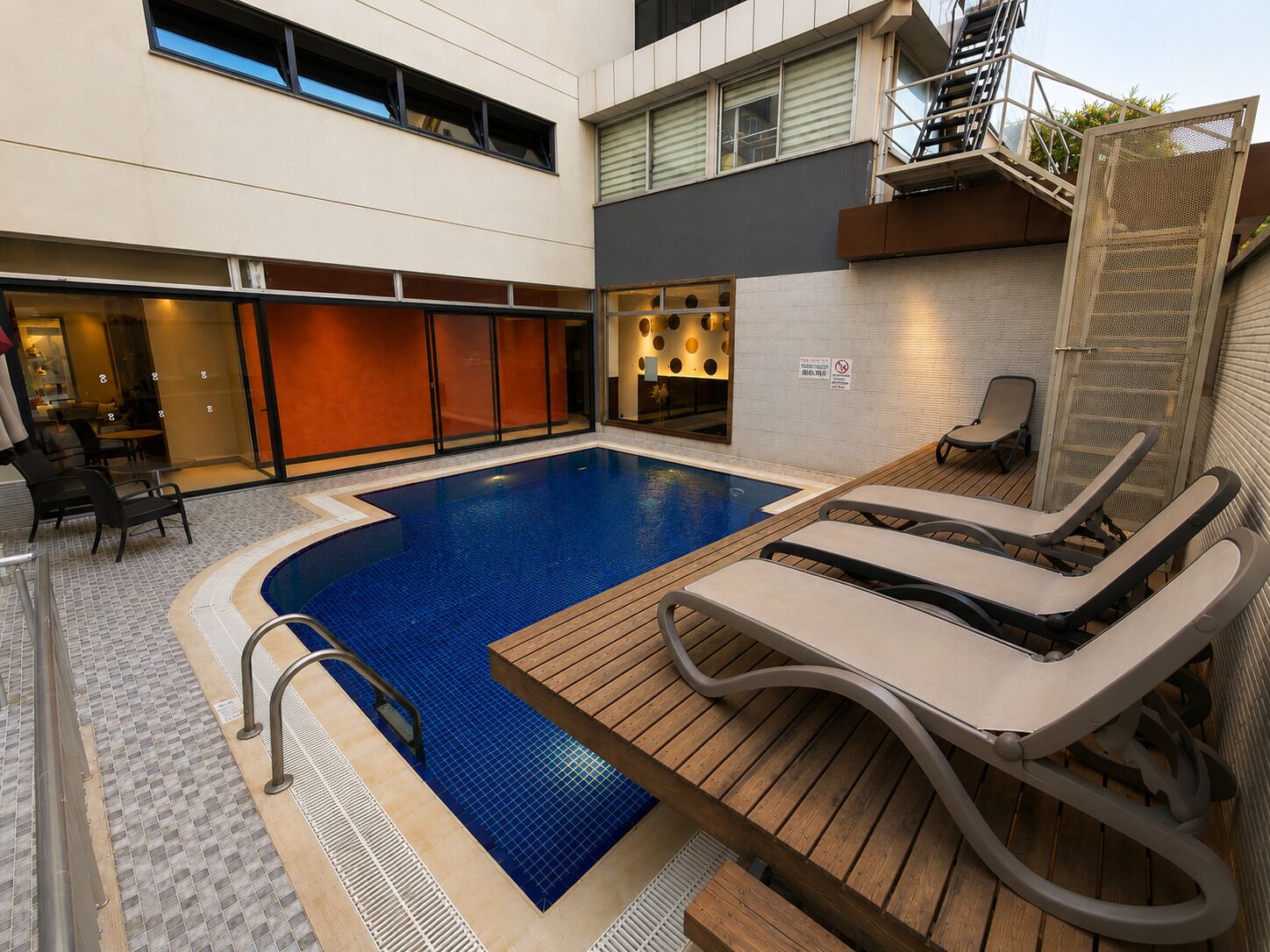 Piscina interior moderna com um deck de madeira, espreguiçadeiras e um espaço com paredes de vidro e vista.