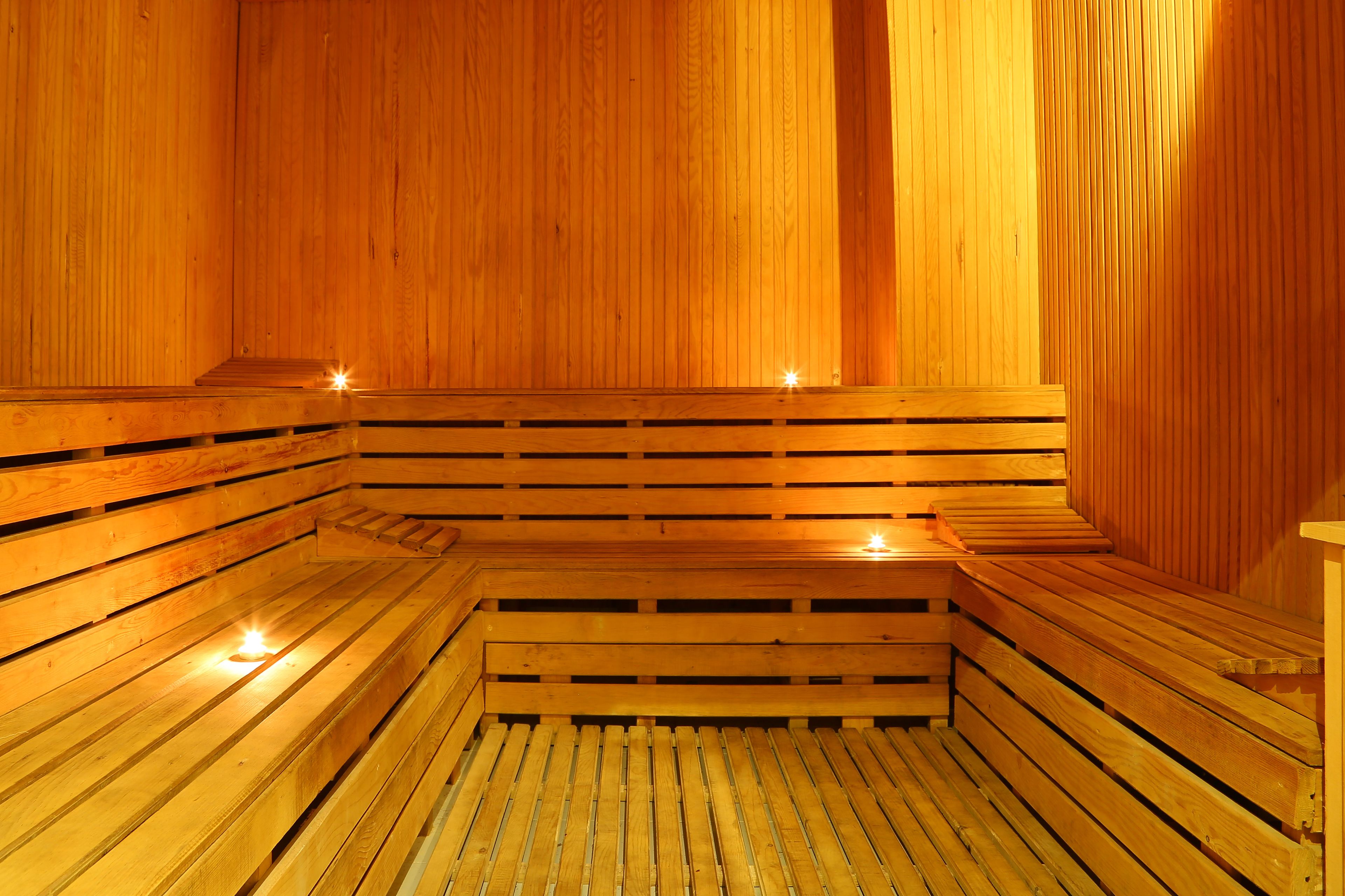 Uma sauna com bancos e paredes de madeira, e um banquinho no canto.