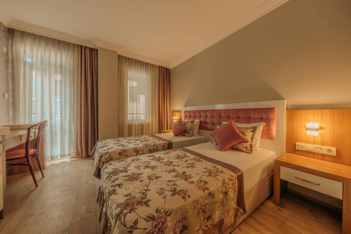 Quarto de hotel com duas camas, uma escrivaninha e uma cadeira.