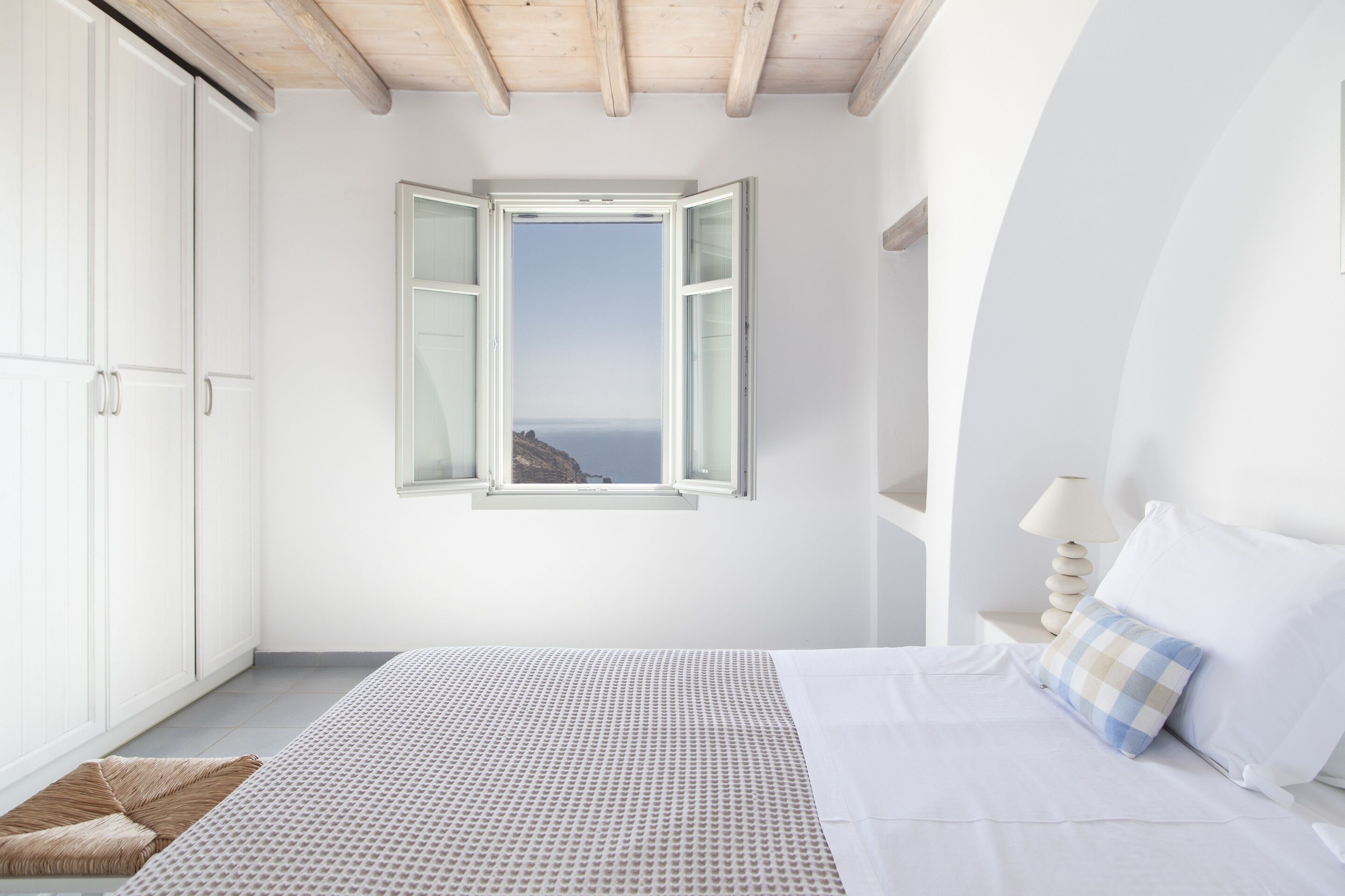 Quarto com cama grande, janela com vista aberta, paredes brancas e teto de madeira.