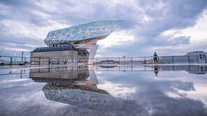 Um edifício moderno com fachada de vidro e design angular único, refletindo em uma superfície molhada.