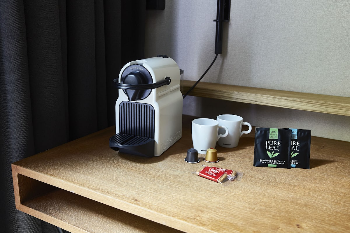 Uma máquina de café, duas xícaras brancas e dois pacotes de chá Pure Leaf sobre uma mesa de madeira.