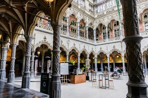 Um interior ornamentado com tetos altos, colunas arqueadas e uma área central de estar com mesas e cadeiras.