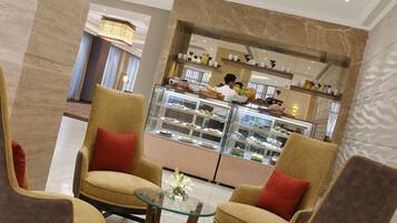Um lobby de hotel moderno com assentos, uma vitrine de vidro com pâtisseries e um teto decorativo.