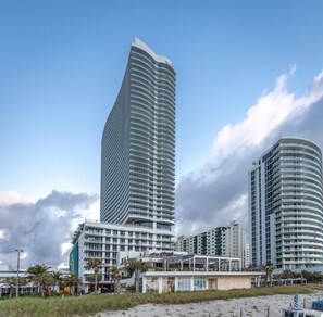 Um hotel moderno com fachada curva, várias varandas e localização à beira-mar.