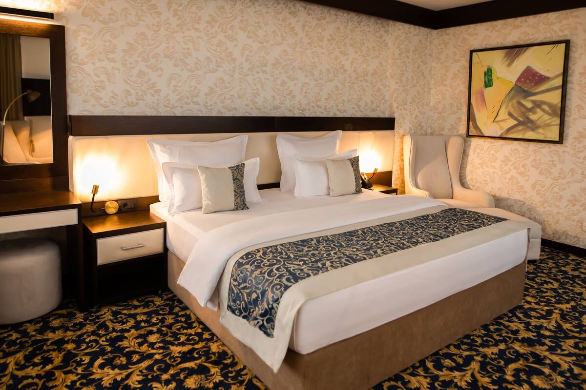 Quarto de hotel com uma cama grande, mesa de cabeceira, escrivaninha e uma cadeira.