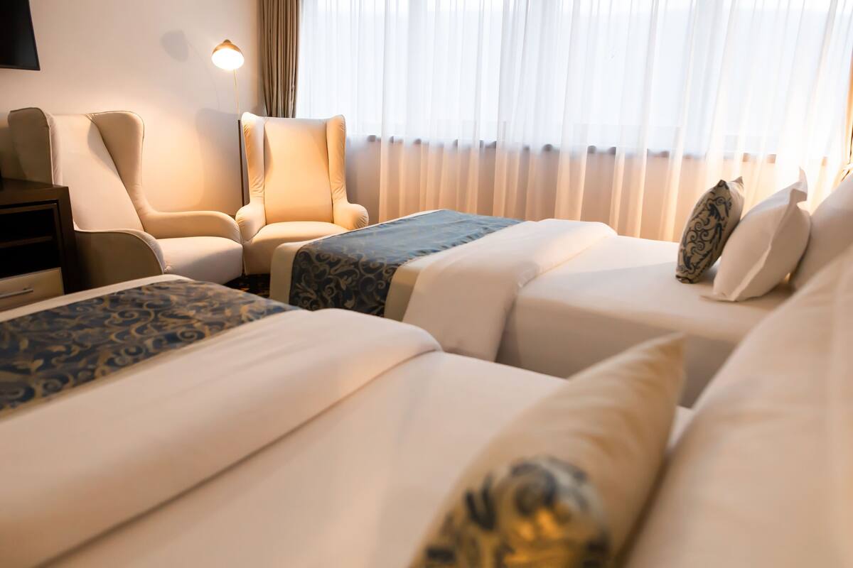 Quarto de hotel com duas camas, uma escrivaninha e uma cadeira.