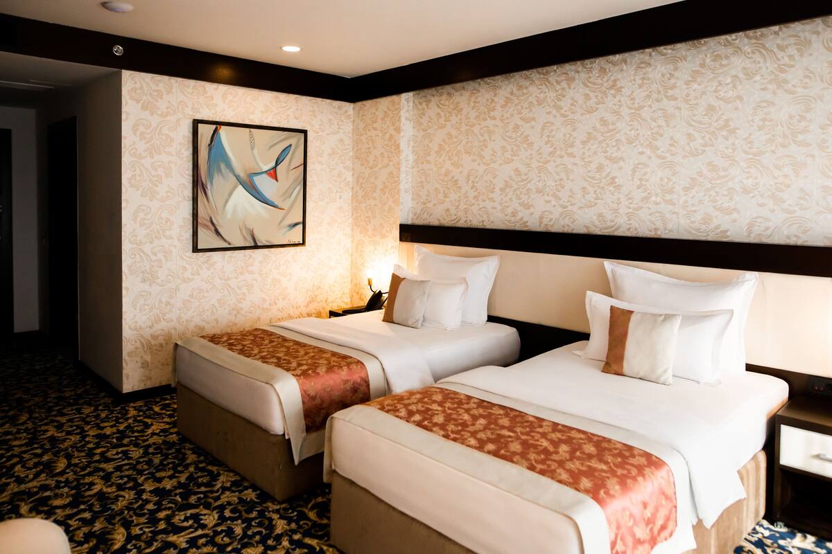Quarto de hotel com duas camas, um quadro grande na parede e papel de parede estampado.