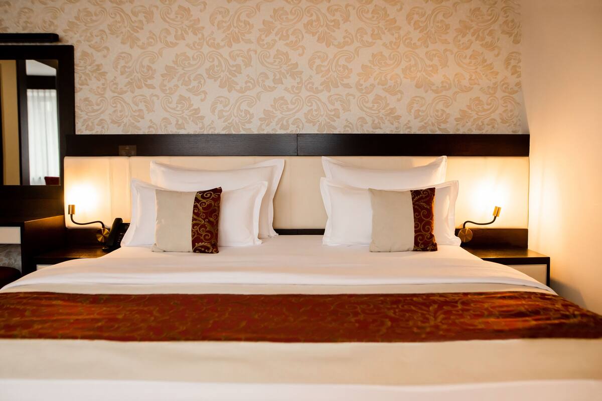 Quarto de hotel com uma cama grande, duas mesas de cabeceira e um espelho.