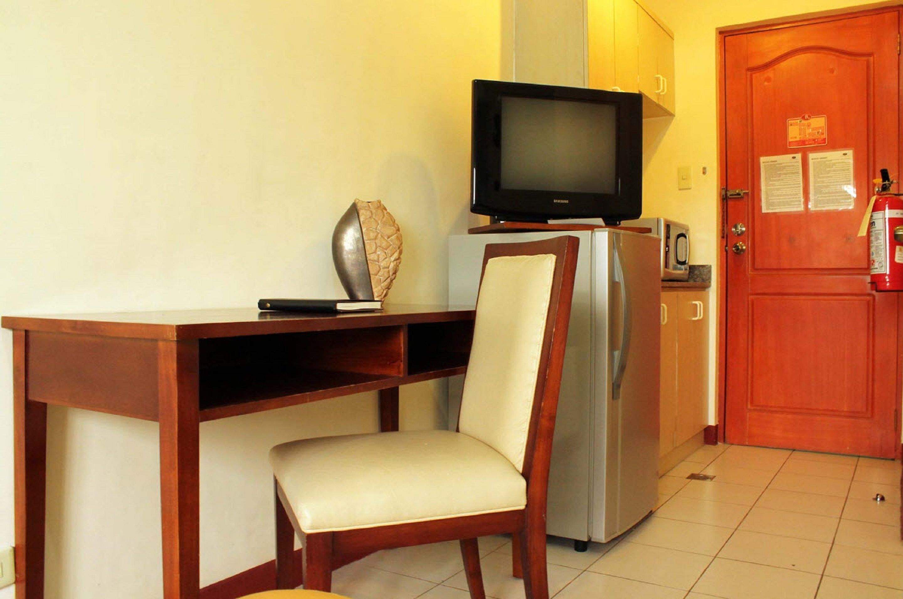 Uma cozinha compacta com frigorífico, micro-ondas e uma televisão por cima.
