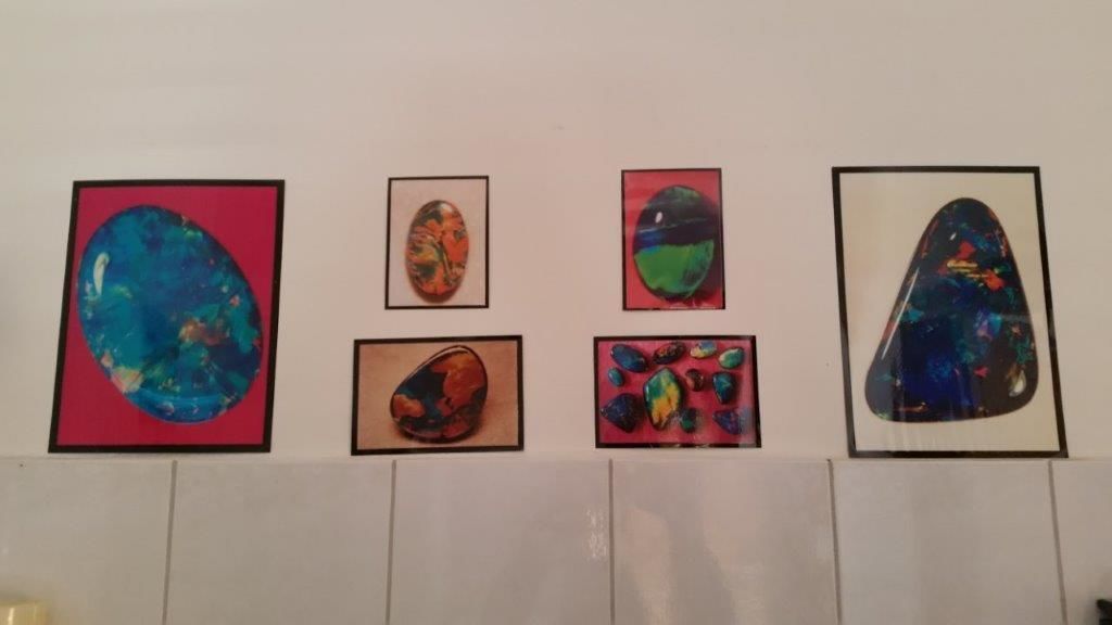 Uma parede com seis obras de arte emolduradas, de diferentes formatos e cores.