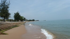 Uma praia com escadas que descem até a água, um cais ao longe e árvores ao longo da costa.
