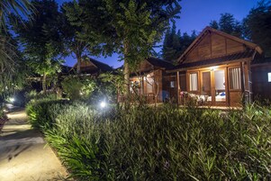 Uma cabana de madeira com varanda, rodeada por vegetação exuberante e um caminho que a leva.