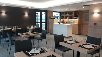 Uma área de refeições moderna com mesas preparadas para dois, completa com taças de vinho e talheres.