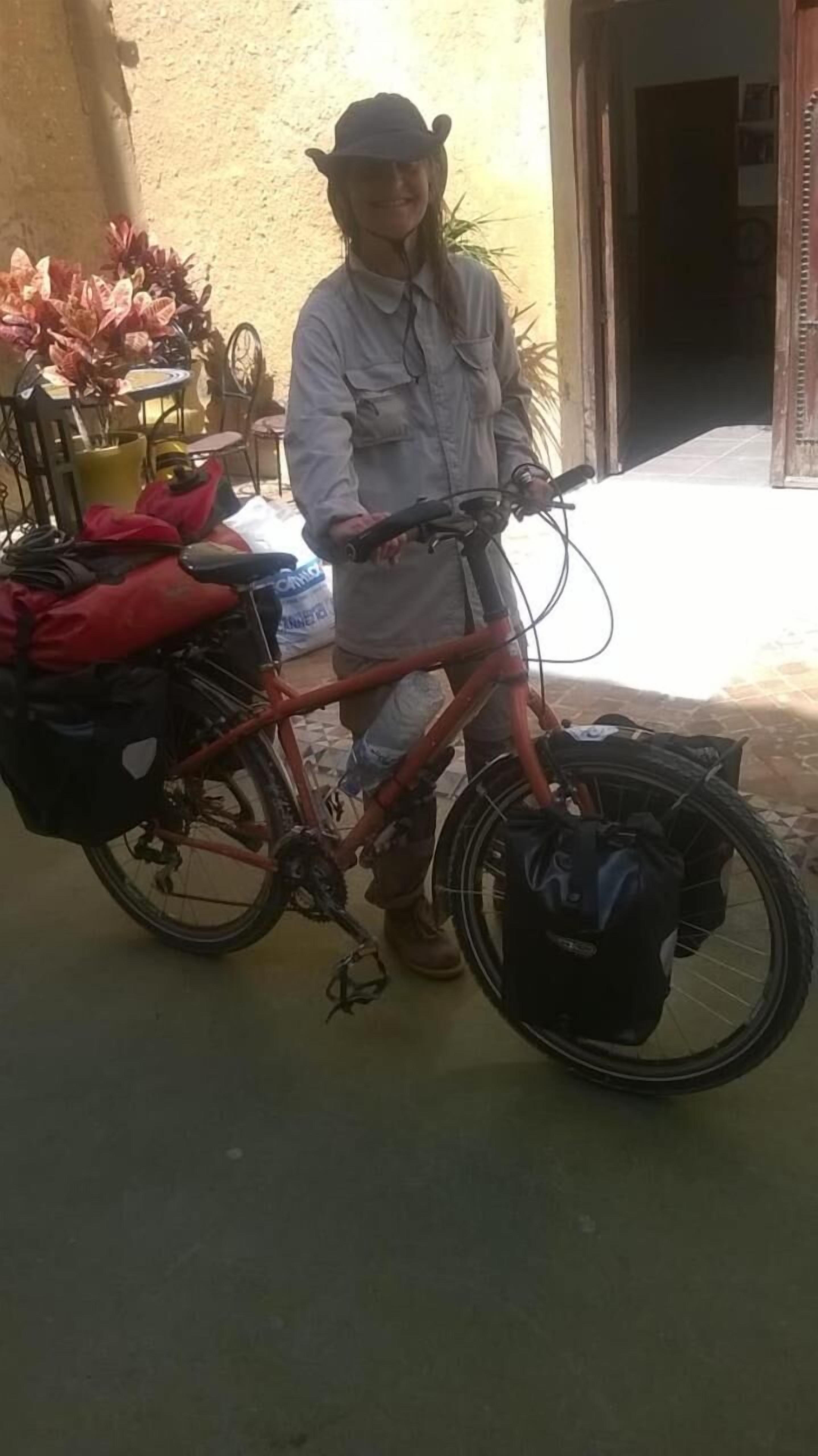 Uma pessoa ao lado de uma bicicleta com estrutura vermelha e uma bolsa preta presa à frente.