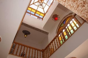Interior com vários níveis, escada, claraboia e elementos decorativos nas paredes.