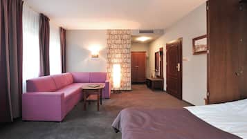 Quarto de hotel com cama, sofá, mesinha, luminária, estante e guarda-roupa.