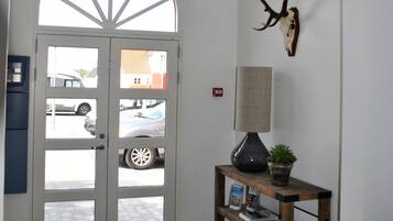 Uma área de recepção com porta dupla, mesa consola de madeira com abajur e um crânio de veado fixado na parede.