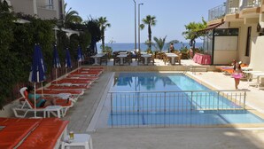 Uma área à beira da piscina com espreguiçadeiras, guarda-sóis e vista para o mar.