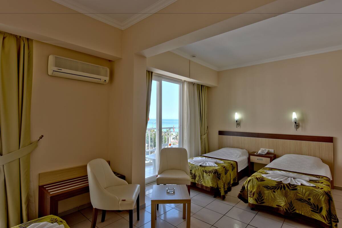 Quarto de hotel com duas camas, uma escrivaninha, uma cadeira e varanda com vista.